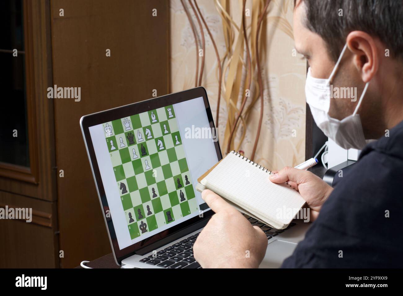 A man in a medical mask solves a chess problem online. Chess board with ...