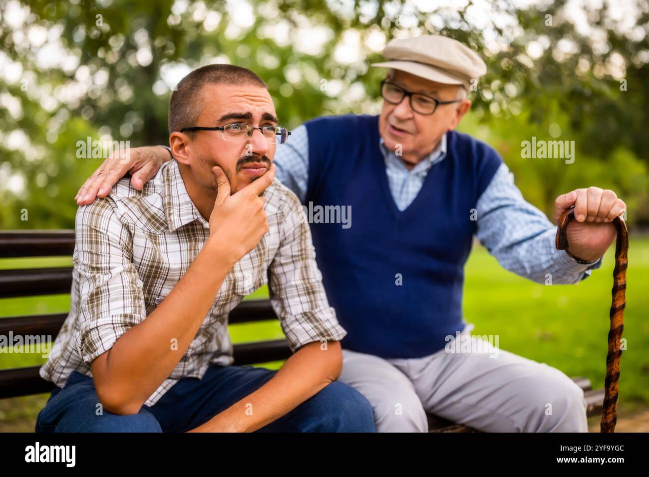 Portrait of grandfather and grandson in park. Young man is worried and ...