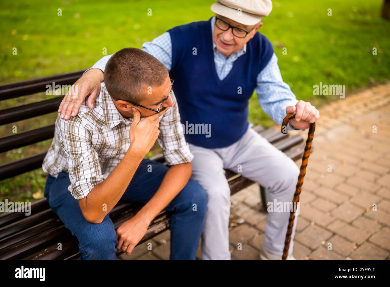 Portrait of grandfather and grandson in park. Young man is worried and ...