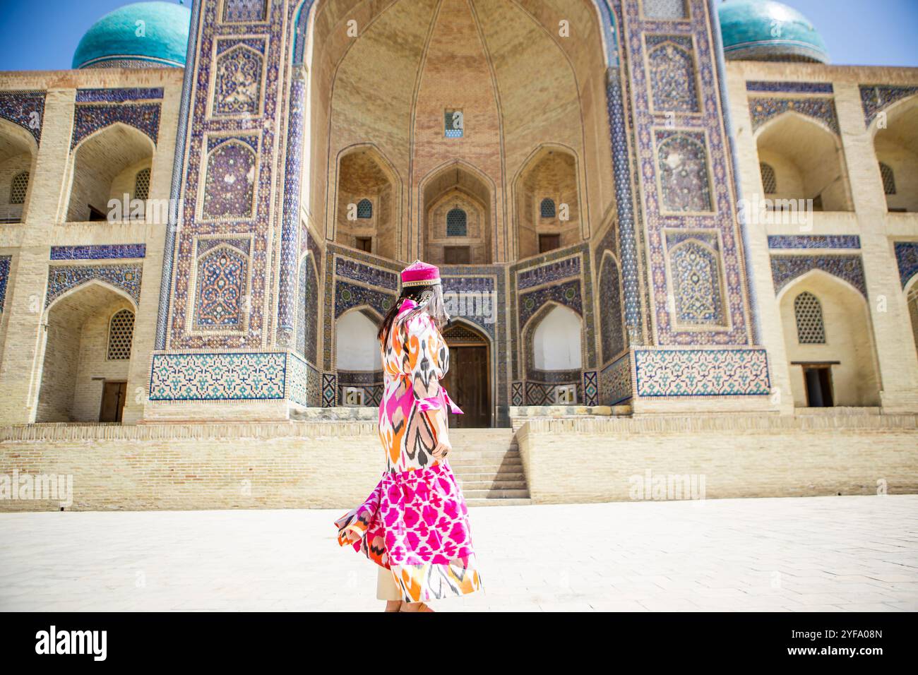 Young woman in traditional Uzbek dress stands facing the Mosque in ...