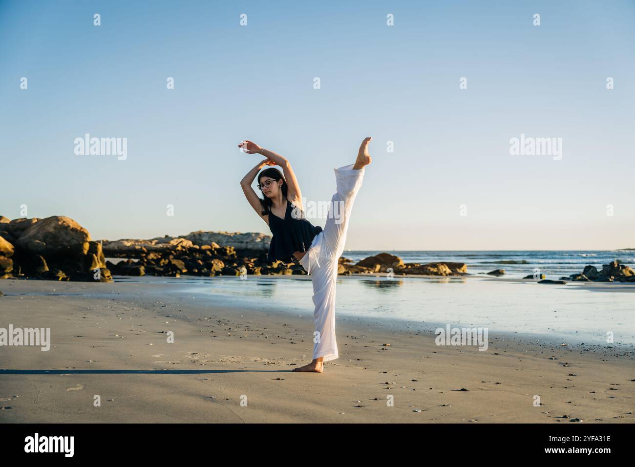 Woman performing a high leg stretch on the beach in graceful pose Stock ...