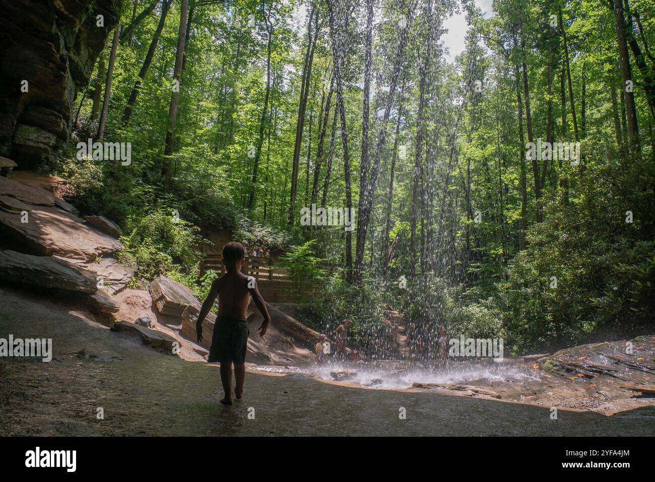 A boy walks on rocks under an overhanging waterfall Stock Photo - Alamy