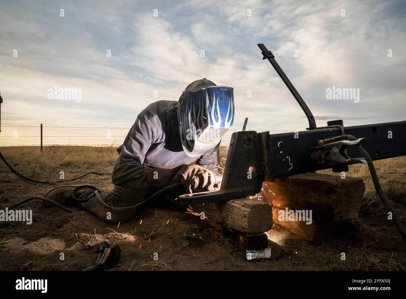 A man in a welding helmet welds a trailer hitch on a farm Stock Photo ...
