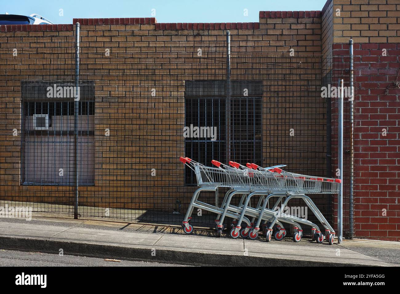 Five wire shopping trolleys stacked together in front of a mesh fence ...