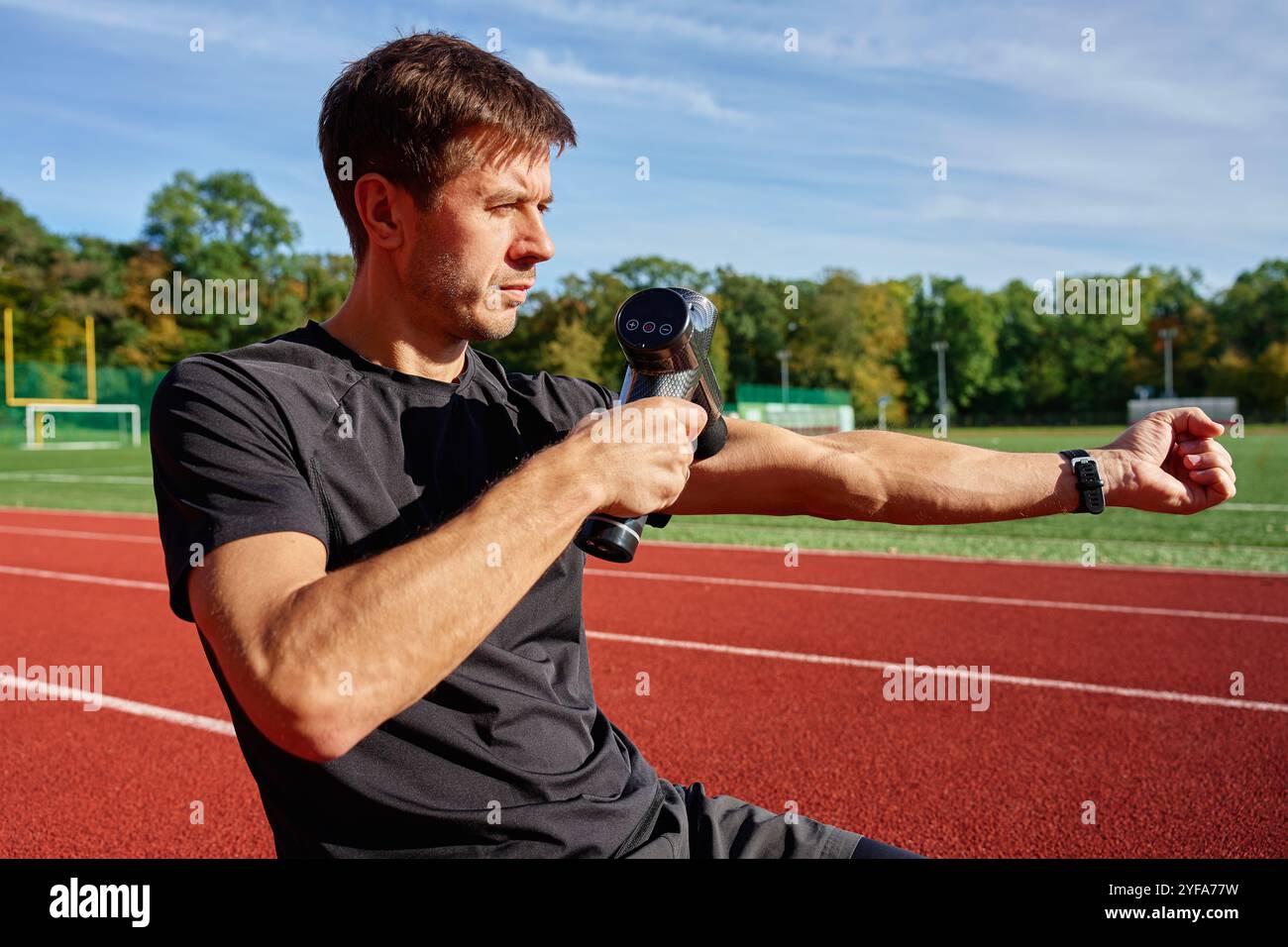 Close-up of male athlete using handheld massage gun on arm muscles for ...