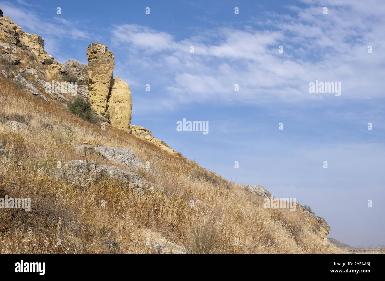 Natural rock formation at the slope of a dry cliff. Cloudy blue sky ...