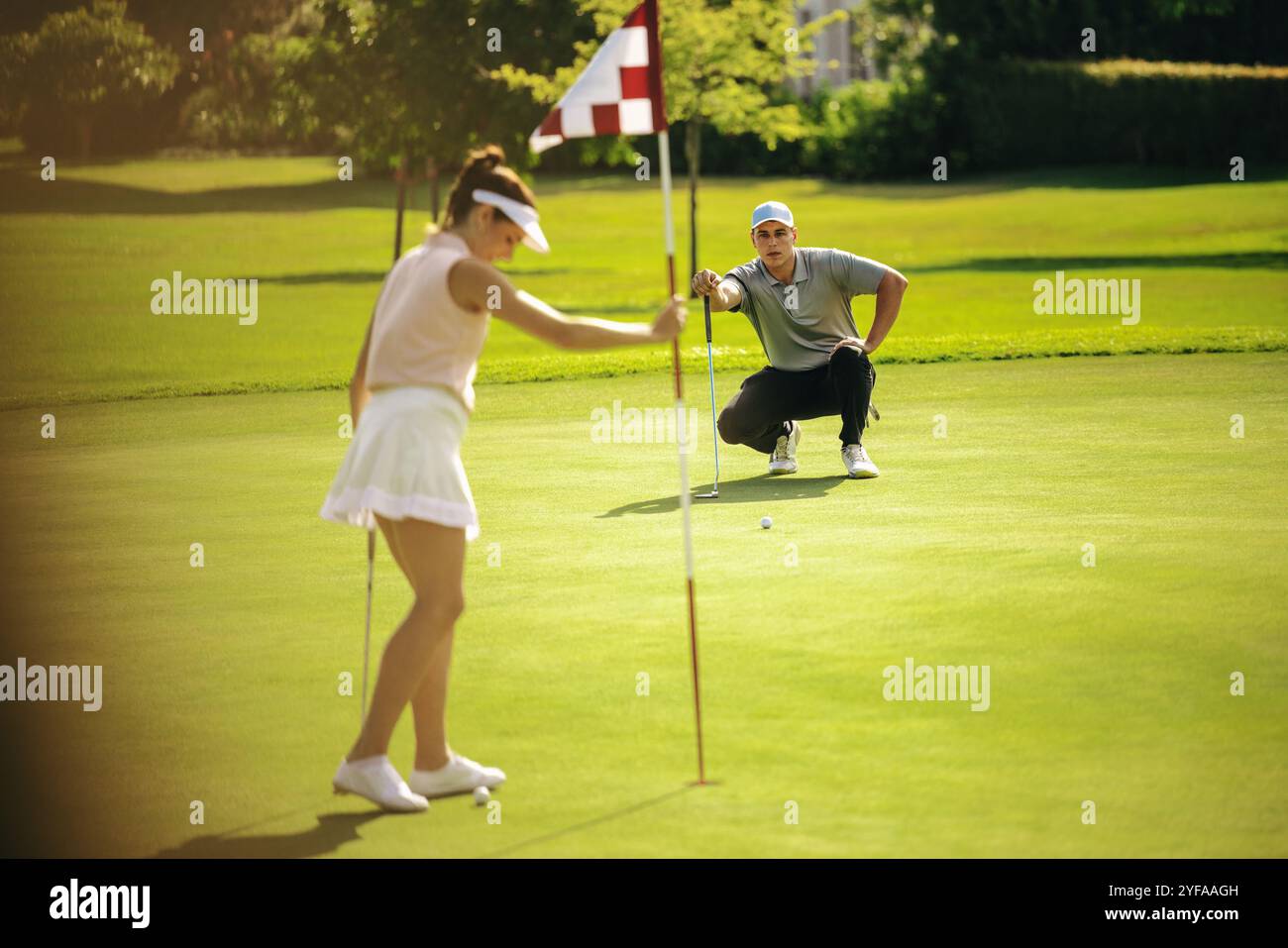 Two golfers on the putting green, with one crouching and aiming near ...