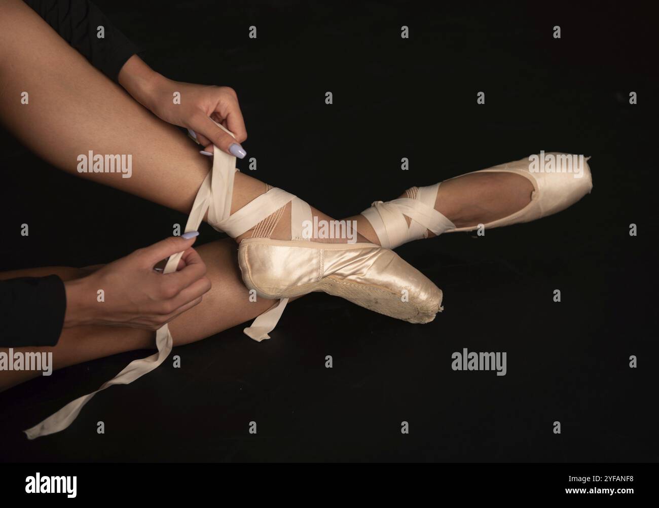 Beautiful legs of young ballerina who puts on pointe shoes at black ...