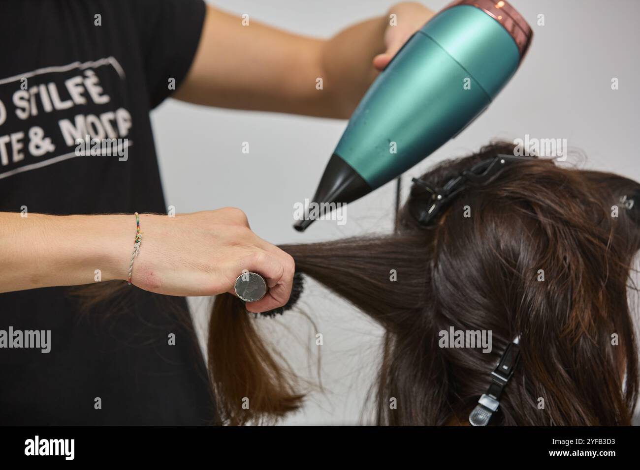 Hair-stylist using hair dryer and brush to style a girl's hair inside a ...