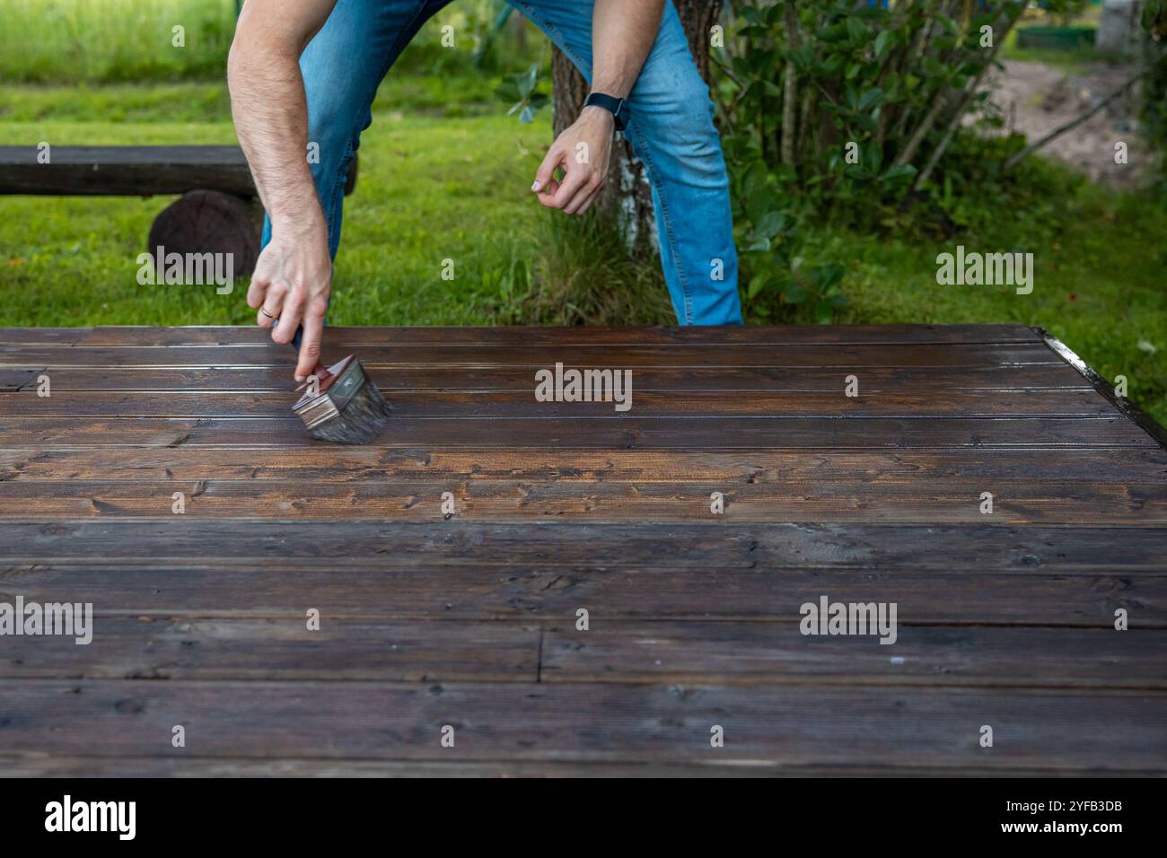 Person applying stain to a wooden deck in a backyard, focusing on ...