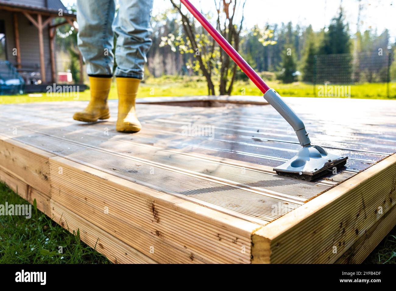 Applying stain to a wooden deck with a brush mop on a sunny day in the ...