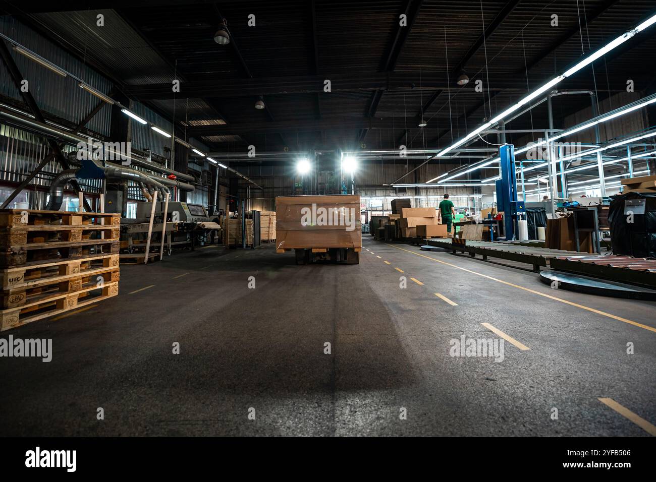 A forklift transporting a large wooden pallet in a spacious warehouse ...