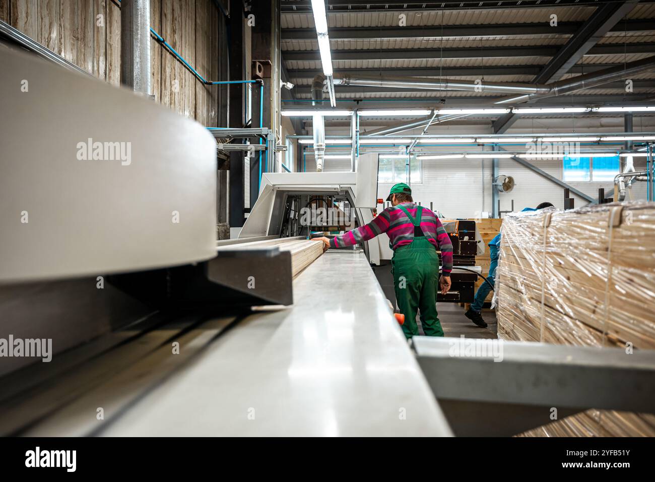 A worker in green overalls operates a machine in a woodworking factory ...