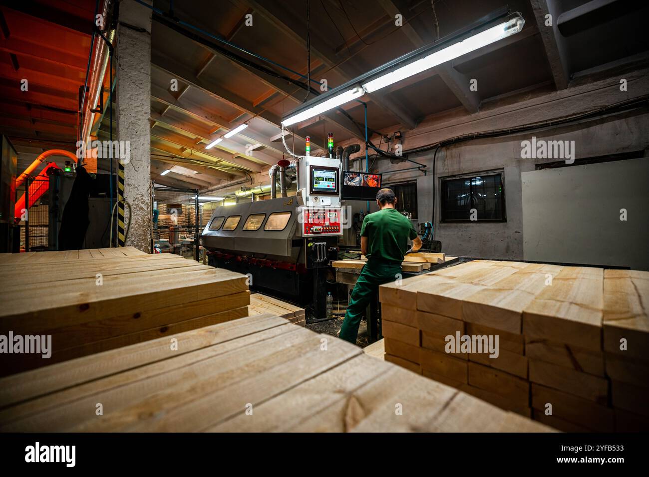 A worker operates a computerized machine in a woodworking factory ...