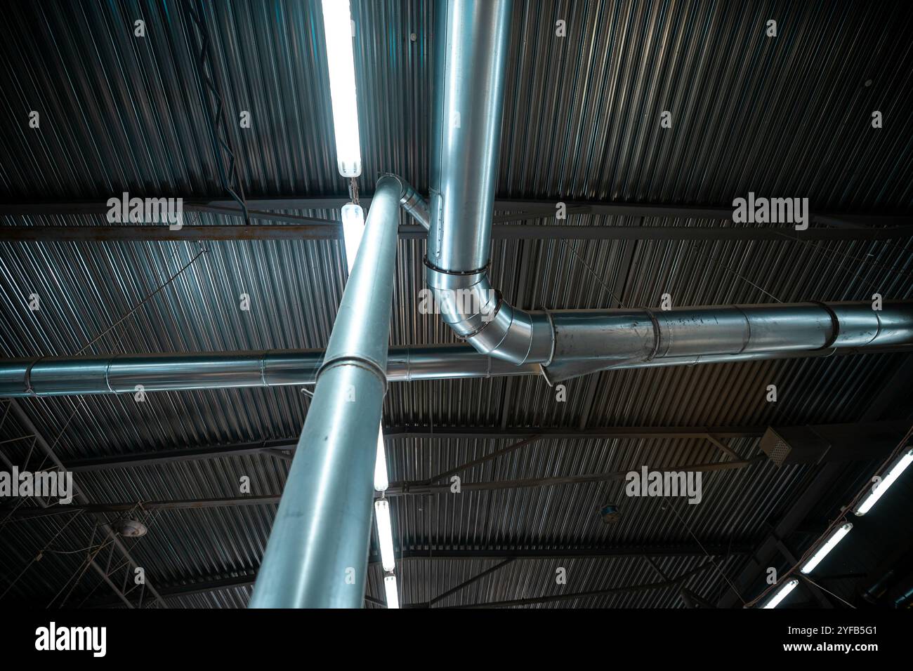 Detailed view of industrial ceiling with metal ducts and bright fluorescent lights, highlighting ...