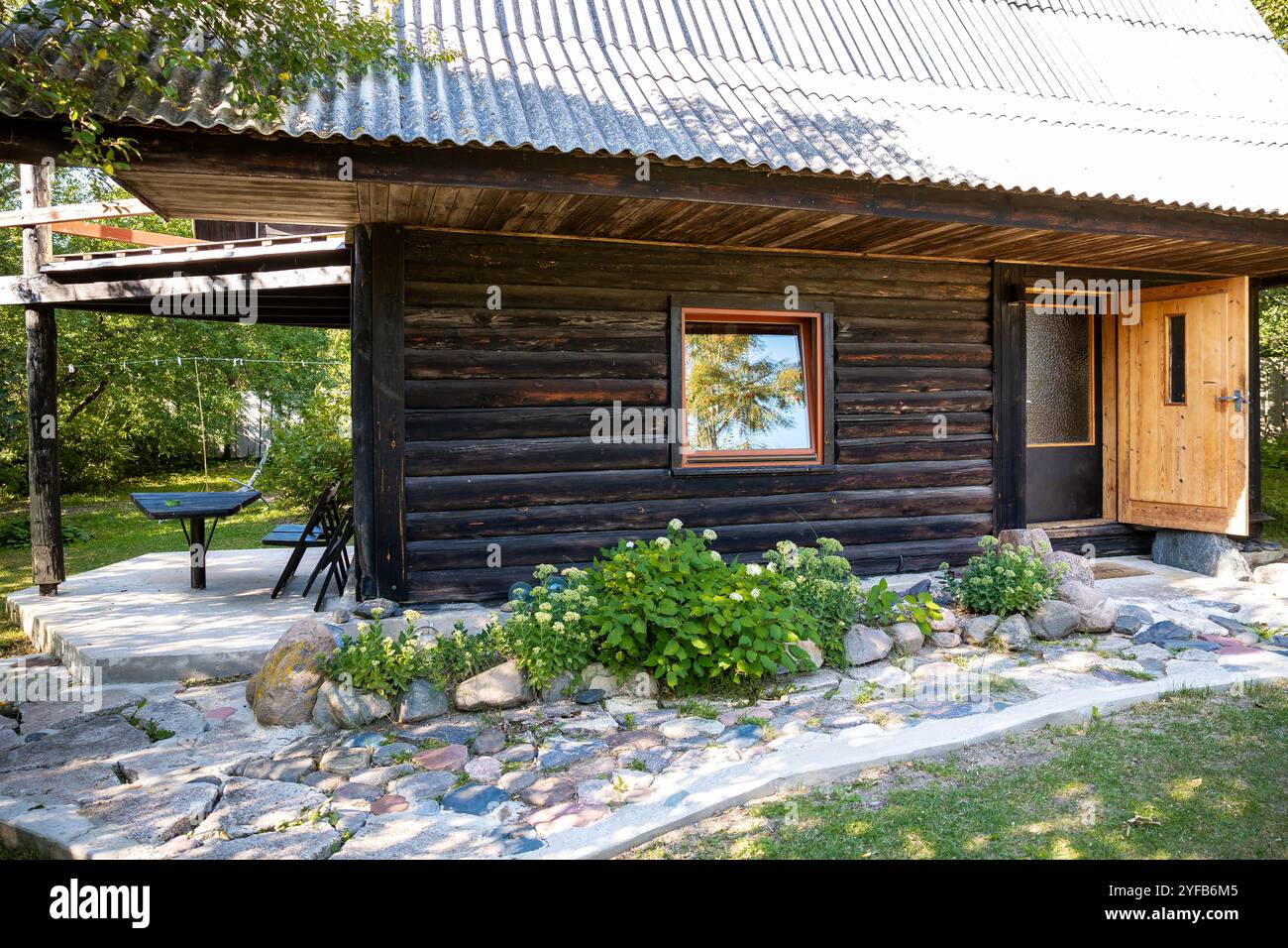 Side view of a rustic wooden cabin with a small porch, surrounded by a ...
