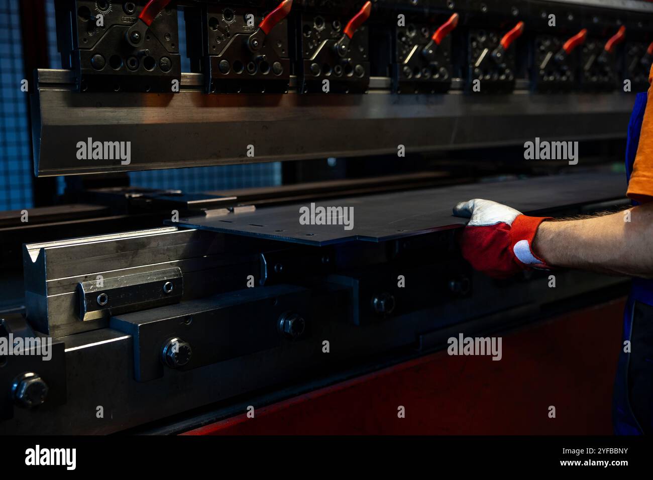 Worker handles a large metal sheet in an industrial press, carefully ...