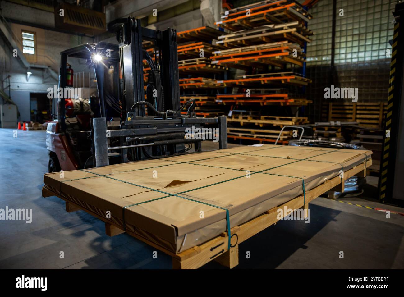 A forklift operates inside a large warehouse, transporting a large ...
