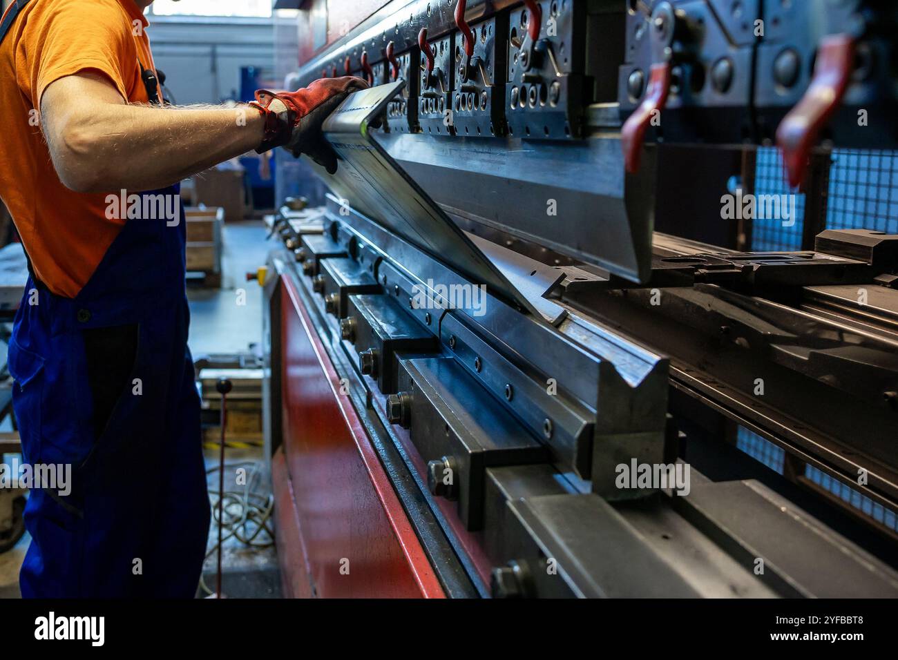Worker adjusts a large metal sheet on an industrial press, ensuring ...