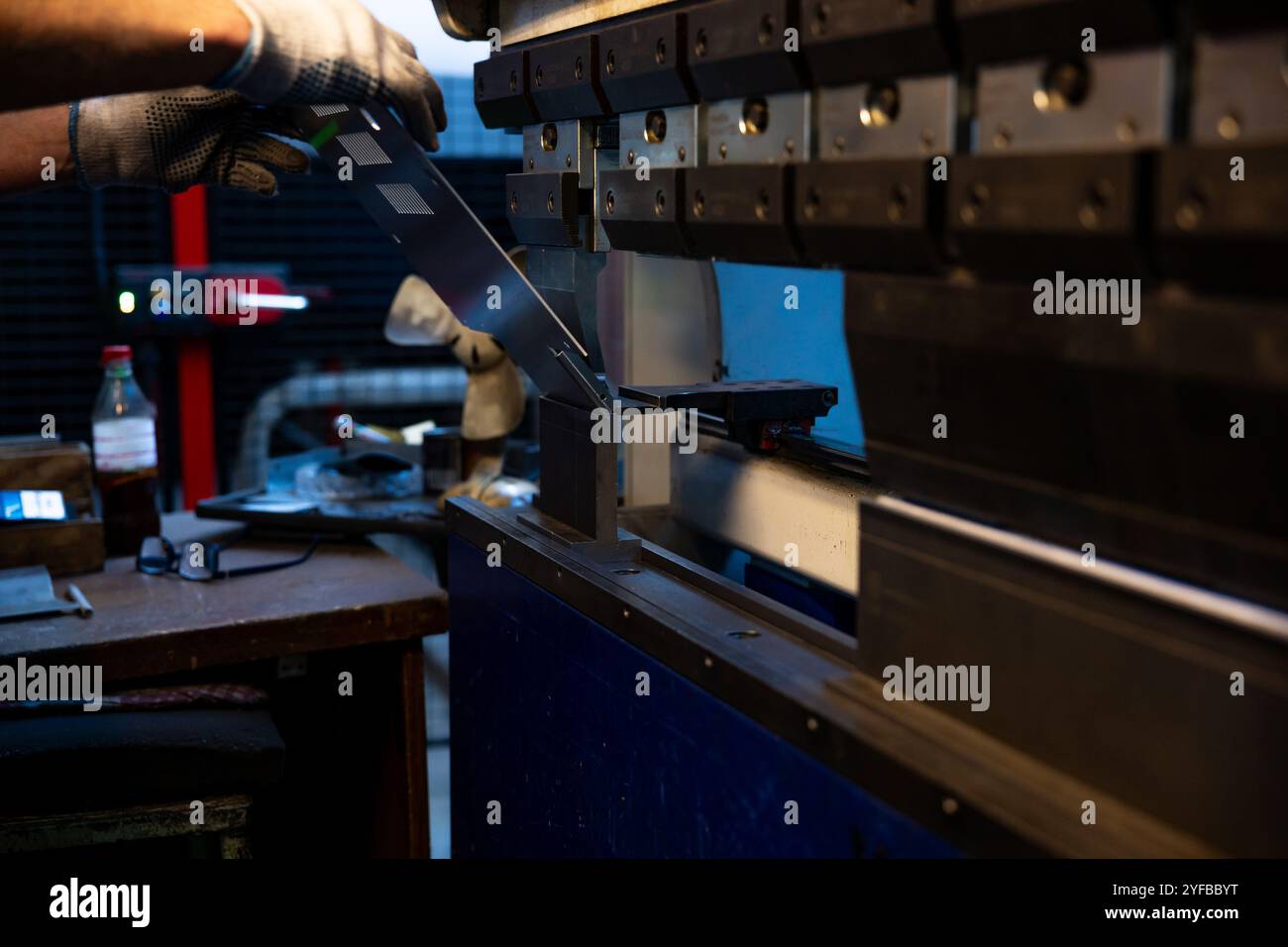 A worker's gloved hands carefully position a metal sheet into an ...
