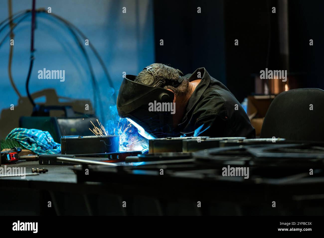 Welder working intently on a metal project, sparks flying from the ...