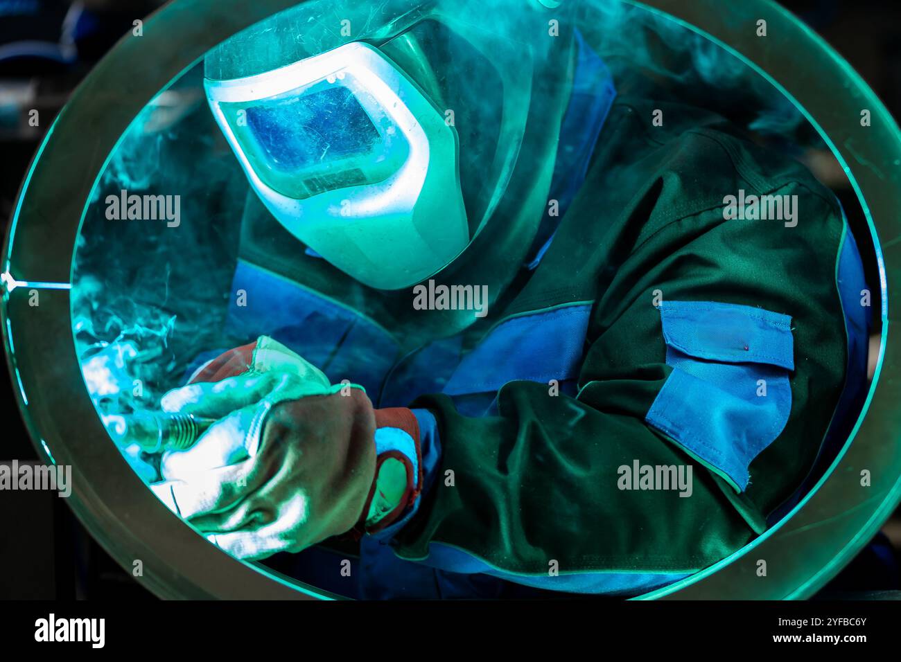 Welder intensely focused on welding a circular metal piece, with bright ...