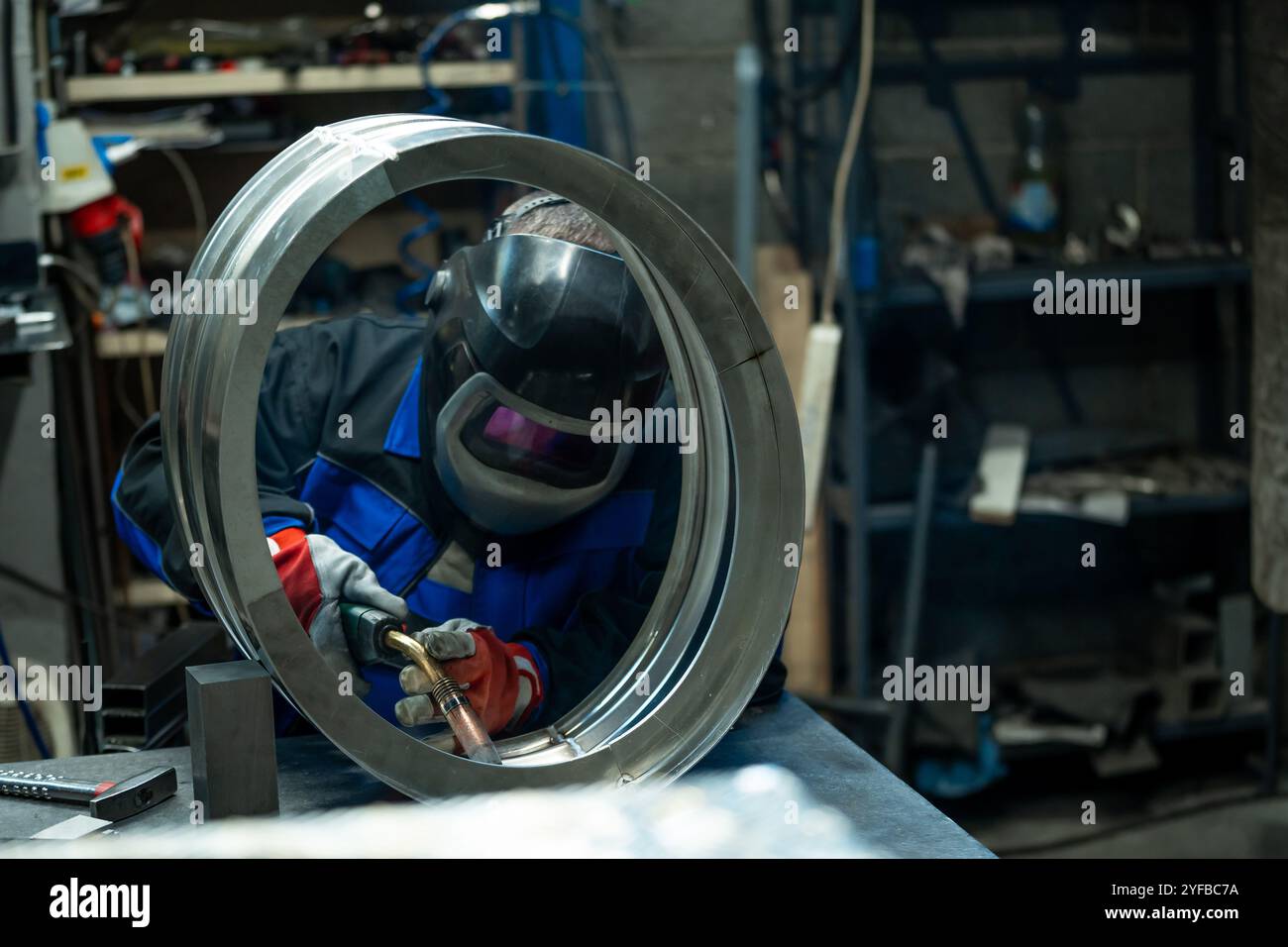 Welder skillfully working on a large metal ring, carefully welding joints in a well-equipped ...