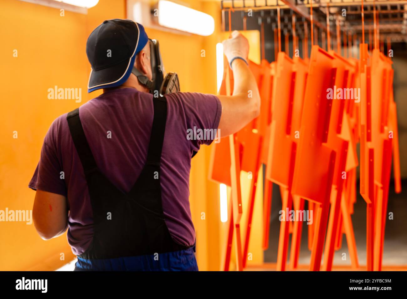 worker in a paint shop, applying a bright orange coat to metal parts ...