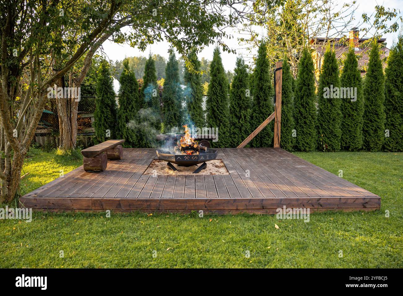 An outdoor wooden deck features a circular fire pit with burning logs ...