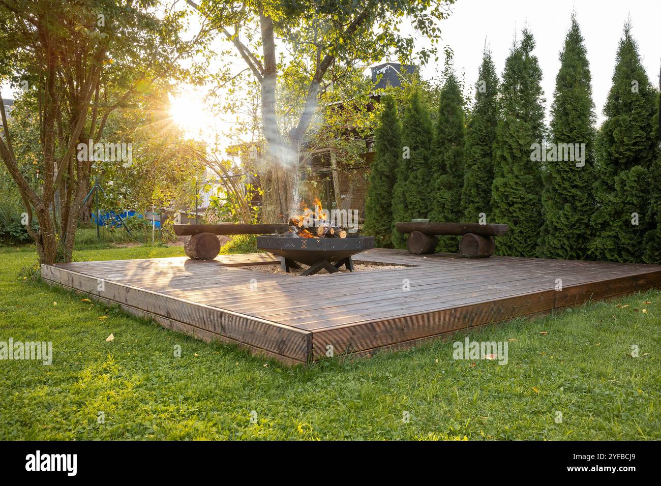 An outdoor wooden deck features a circular fire pit with burning logs ...