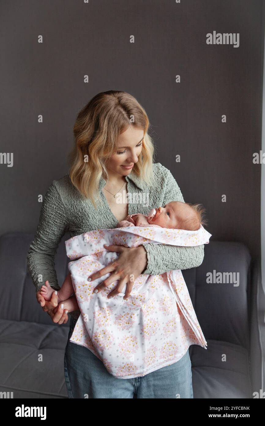 Beautiful blonde mother holds newborn baby in arms wrapped in swaddle ...