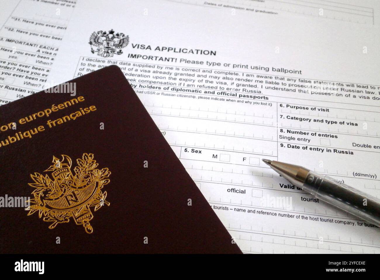 a ballpoint pen and a french passport on the top of a visa application ...