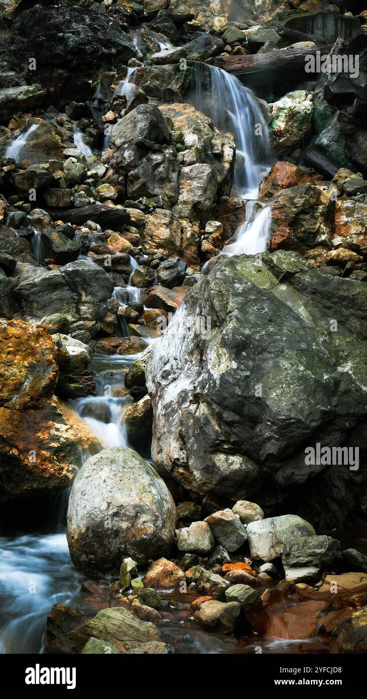 A mini waterfall with rushing water flows over large rocks covered in ...