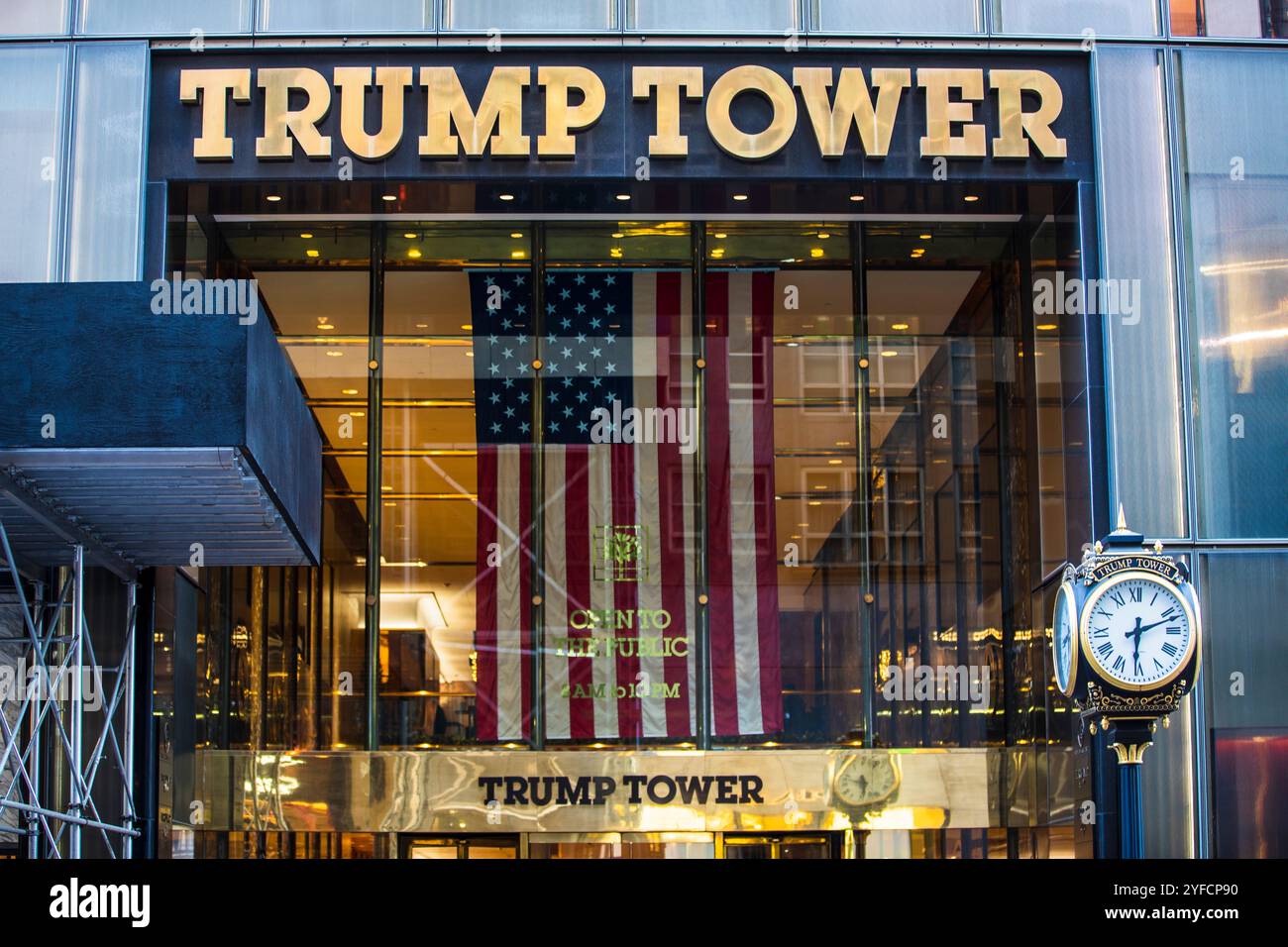 The entrance of Trump Tower in New York City, featuring a clock and a large American flag inside ...