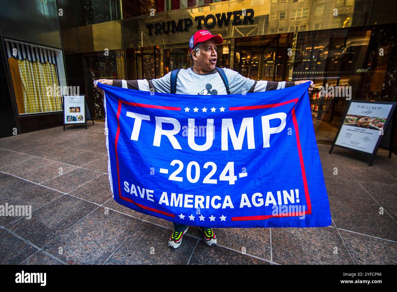 A supporter holding a "Trump 2024 Save America Again!" banner outside ...