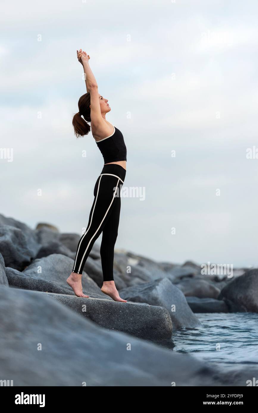 fit sporty woman standing on rocks by the sea doing stretching ...