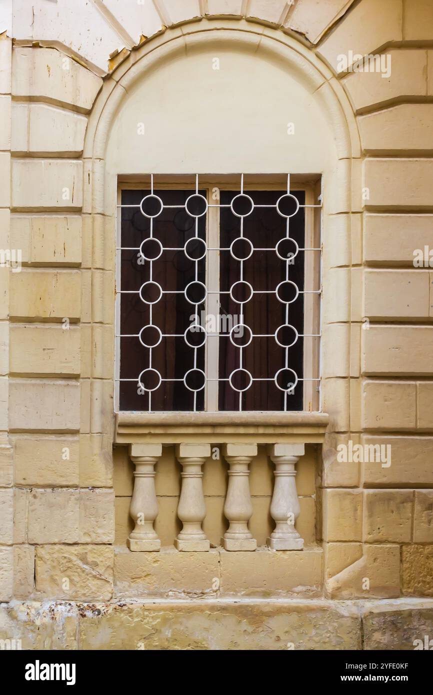 A vintage arched window with an ornate iron grill and stone balustrade ...