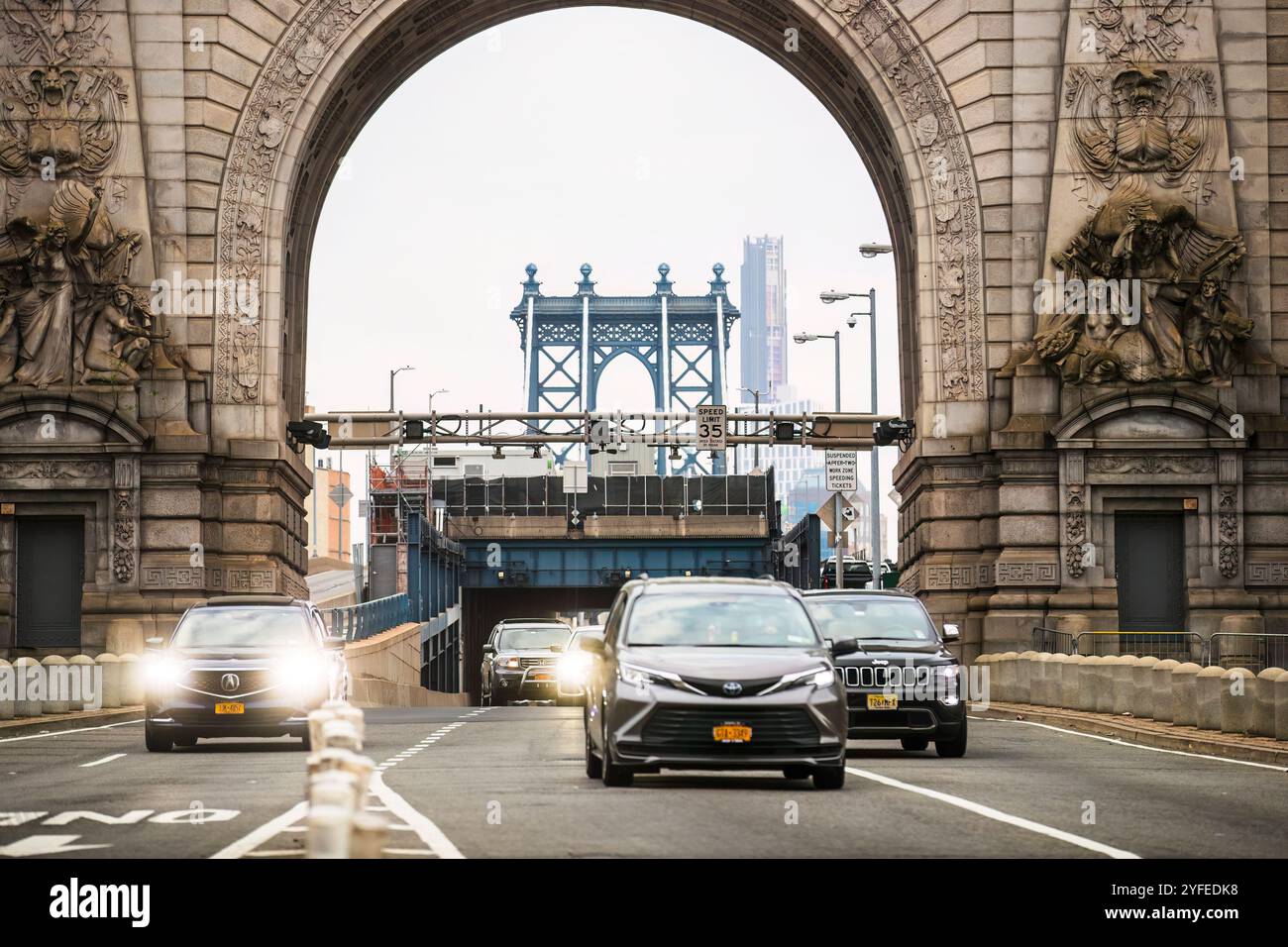 Vehicles drive through the grand arch of the Manhattan Bridge entrance ...