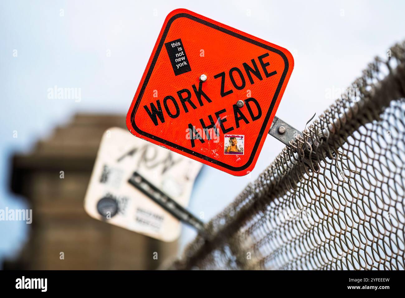 A tilted "Work Zone Ahead" sign with stickers attached is mounted on a ...