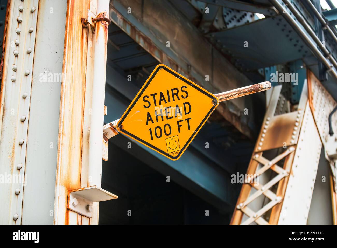 A yellow "Stairs Ahead 100 FT" warning sign is bent and mounted on a ...
