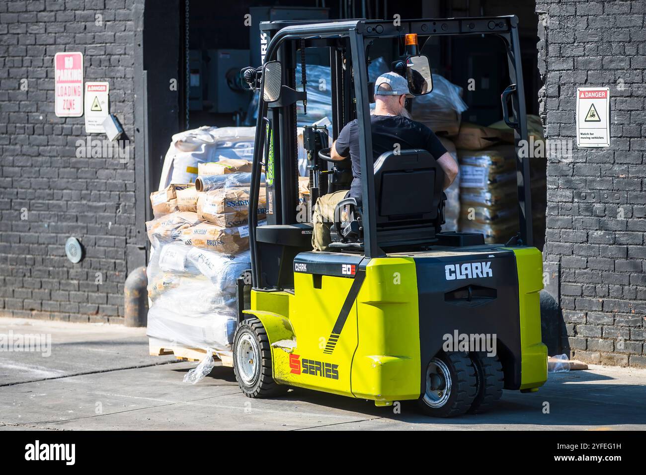 Worker operating a Clark forklift moving a pallet of goods at a loading ...