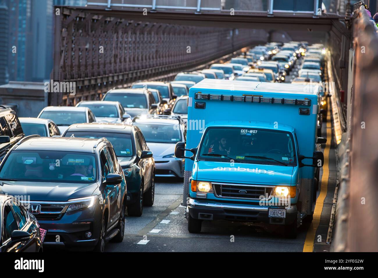 Light blue ambulance navigating through heavy traffic on a bridge in ...