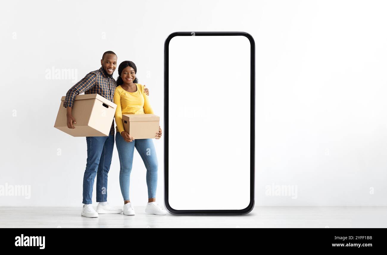 Happy couple posing with cardboard boxes beside a large empty phone ...