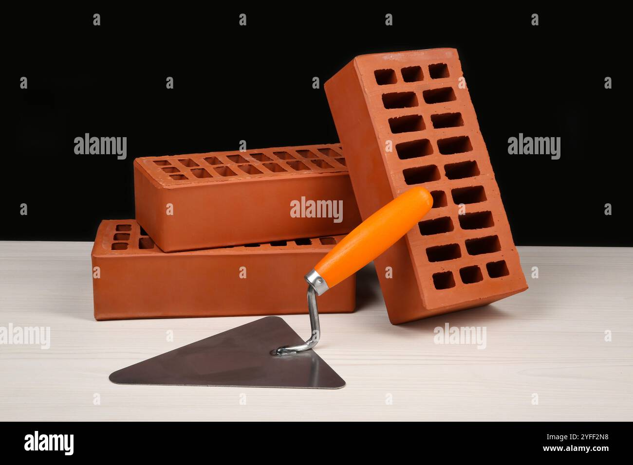 Many red bricks and putty knife on light wooden table against black ...
