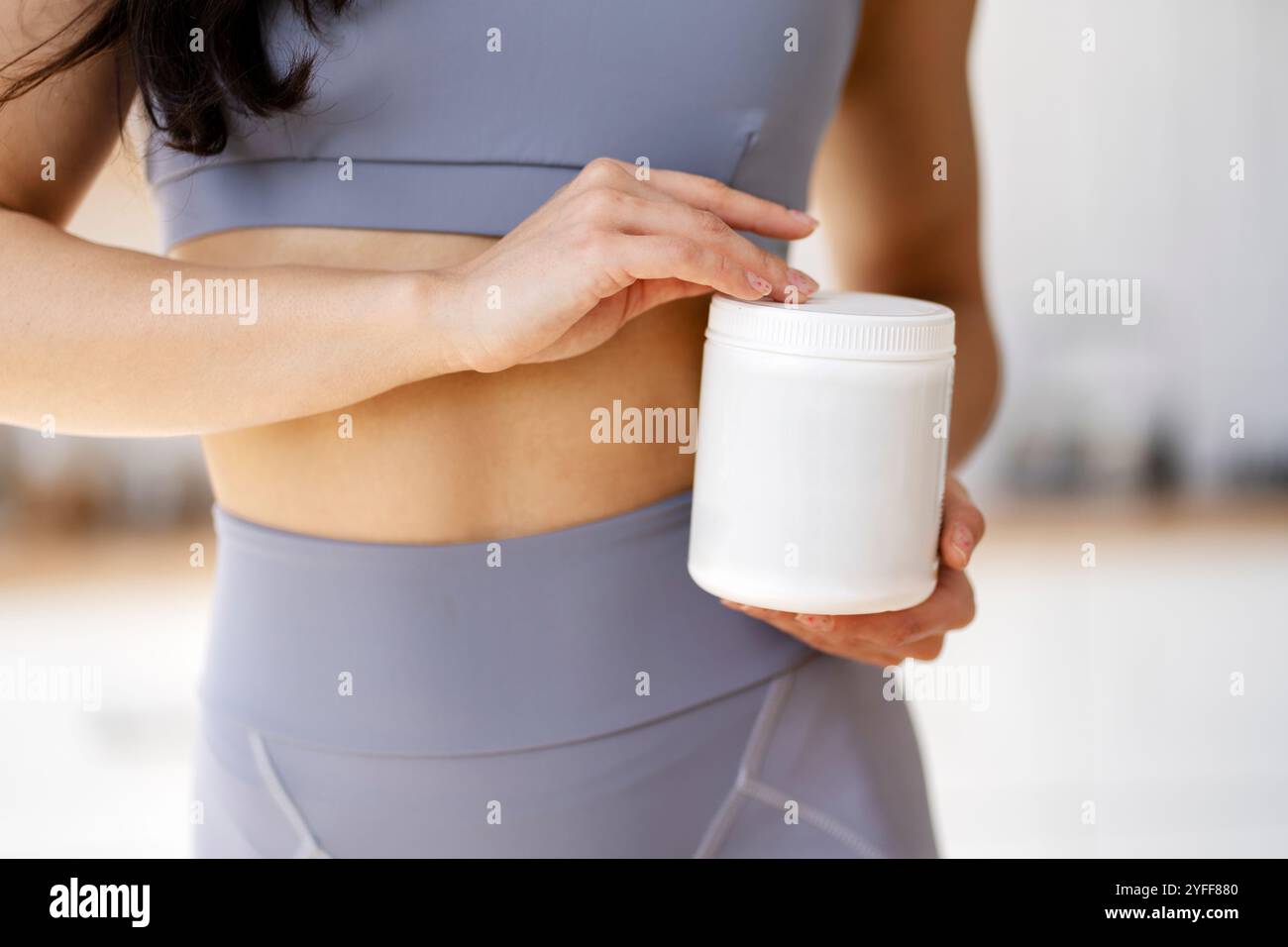 Focused woman in gym post workout, holding white supplement jar ...
