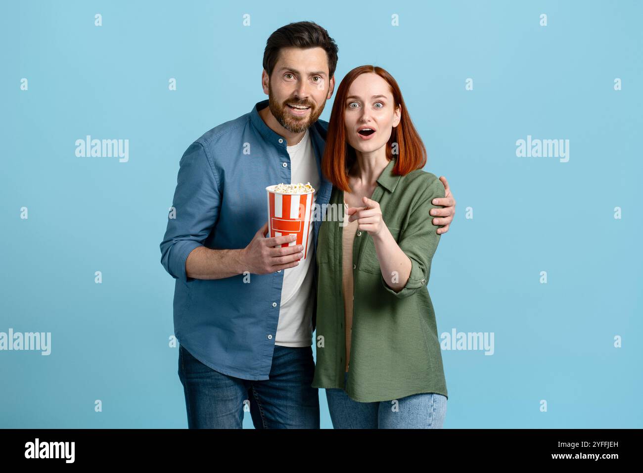 Young couple is holding a bucket of popcorn, the woman is pointing her ...