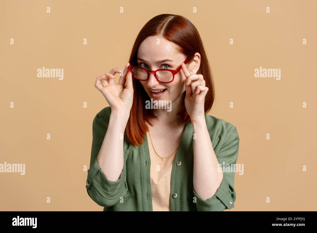 Surprised woman with red hair is adjusting her red glasses with a ...