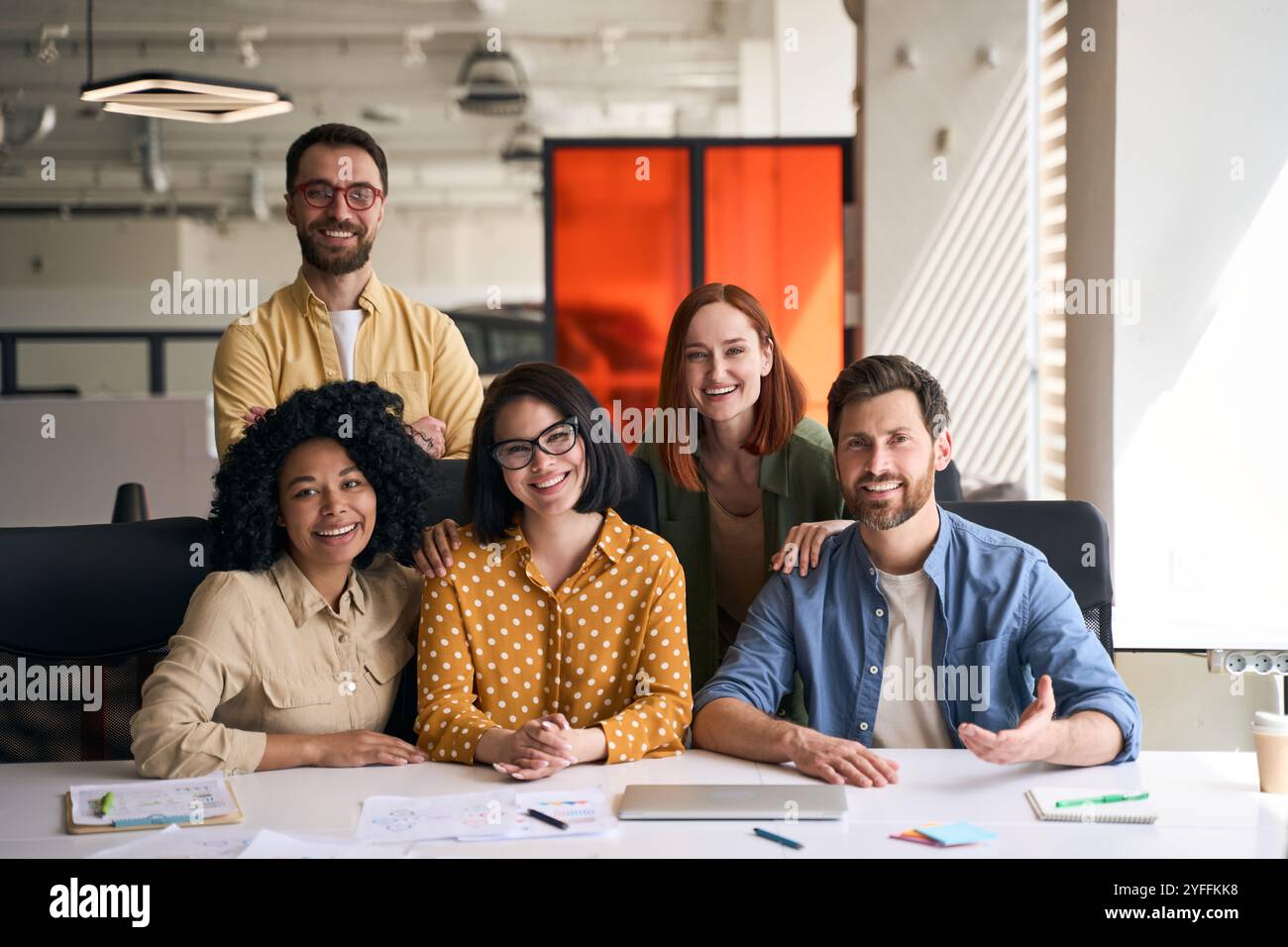 Diverse team of five professionals is smiling while sitting and ...