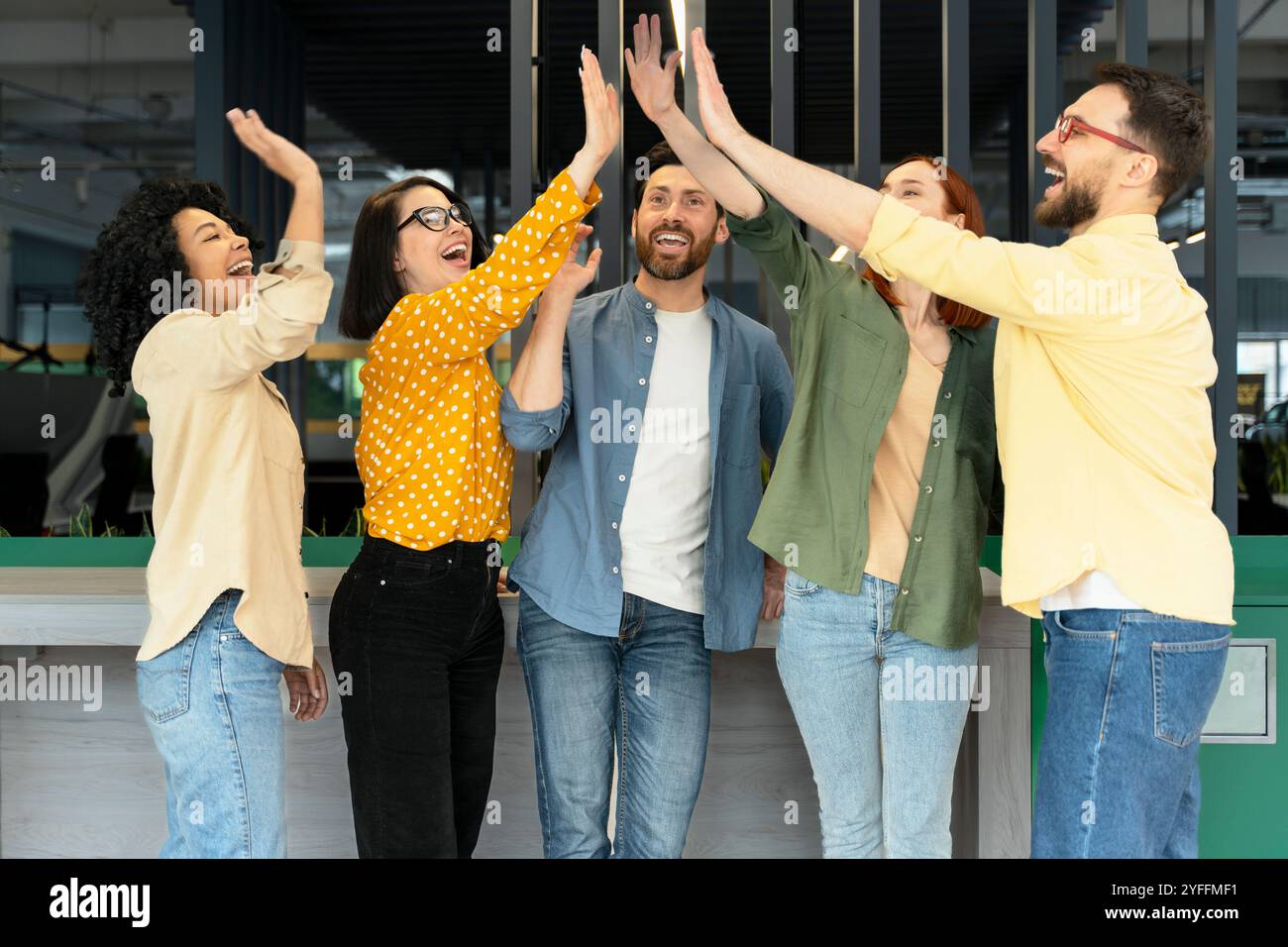 Group of five coworkers are giving a high five while smiling and ...