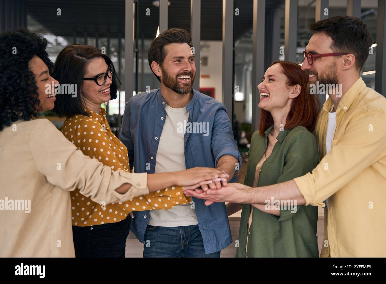 Diverse team of coworkers is putting their hands together, laughing and celebrating a success in ...